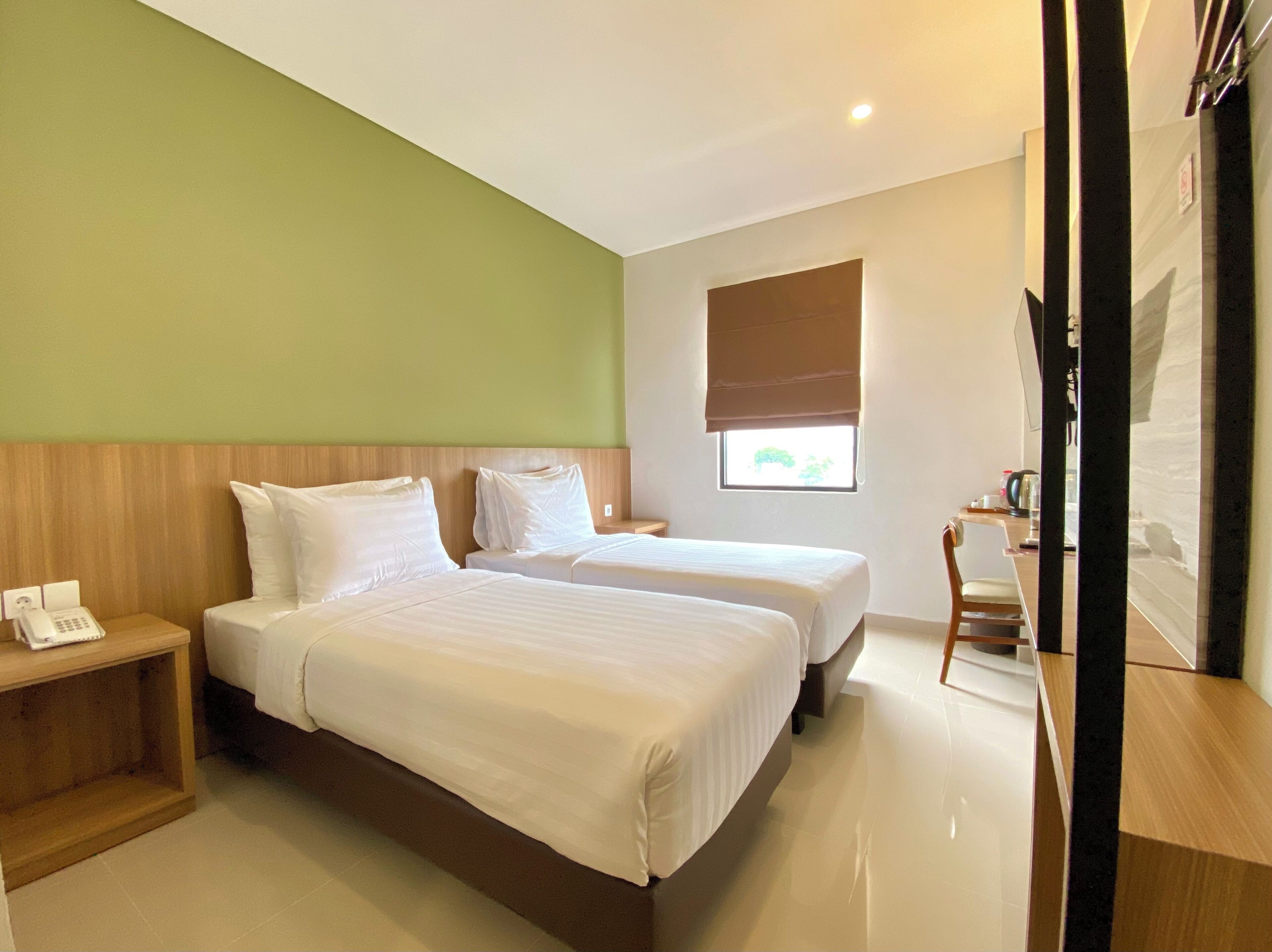Quarto de hotel com duas camas, cabeceira de madeira, mesa de cabeceira com telefone, janela com vista e televisão em suporte.