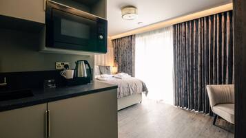 Quarto de hotel moderno com cozinha compacta, uma cama, um sofá e uma janela grande com cortinas.