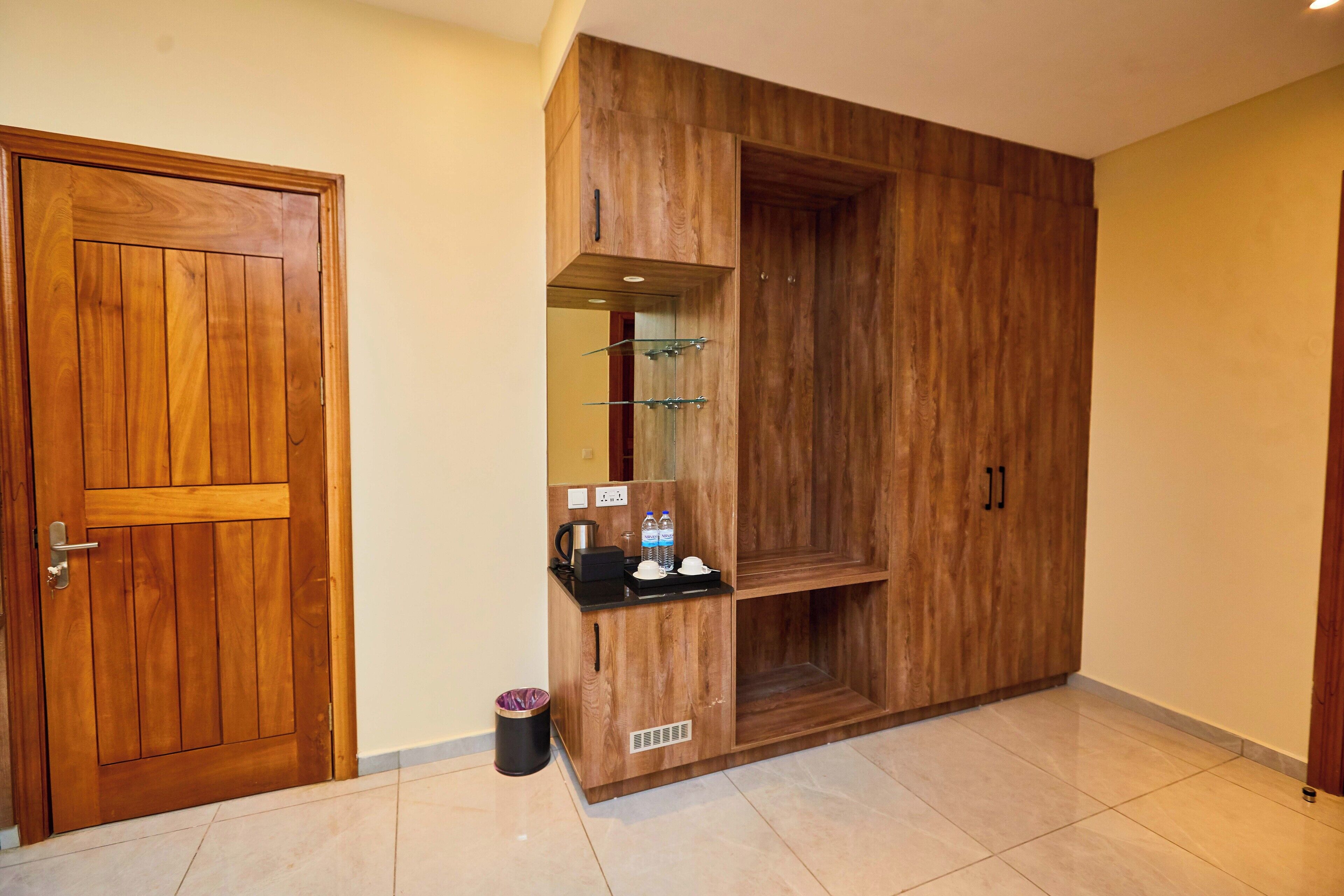 Quarto com guarda-roupa de madeira, uma prateleira pequena com artigos de higiene e uma porta.