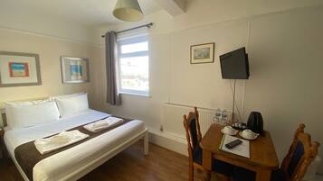 Quarto de hotel com cama, mesa, cadeira, televisão e janela com cortinas.