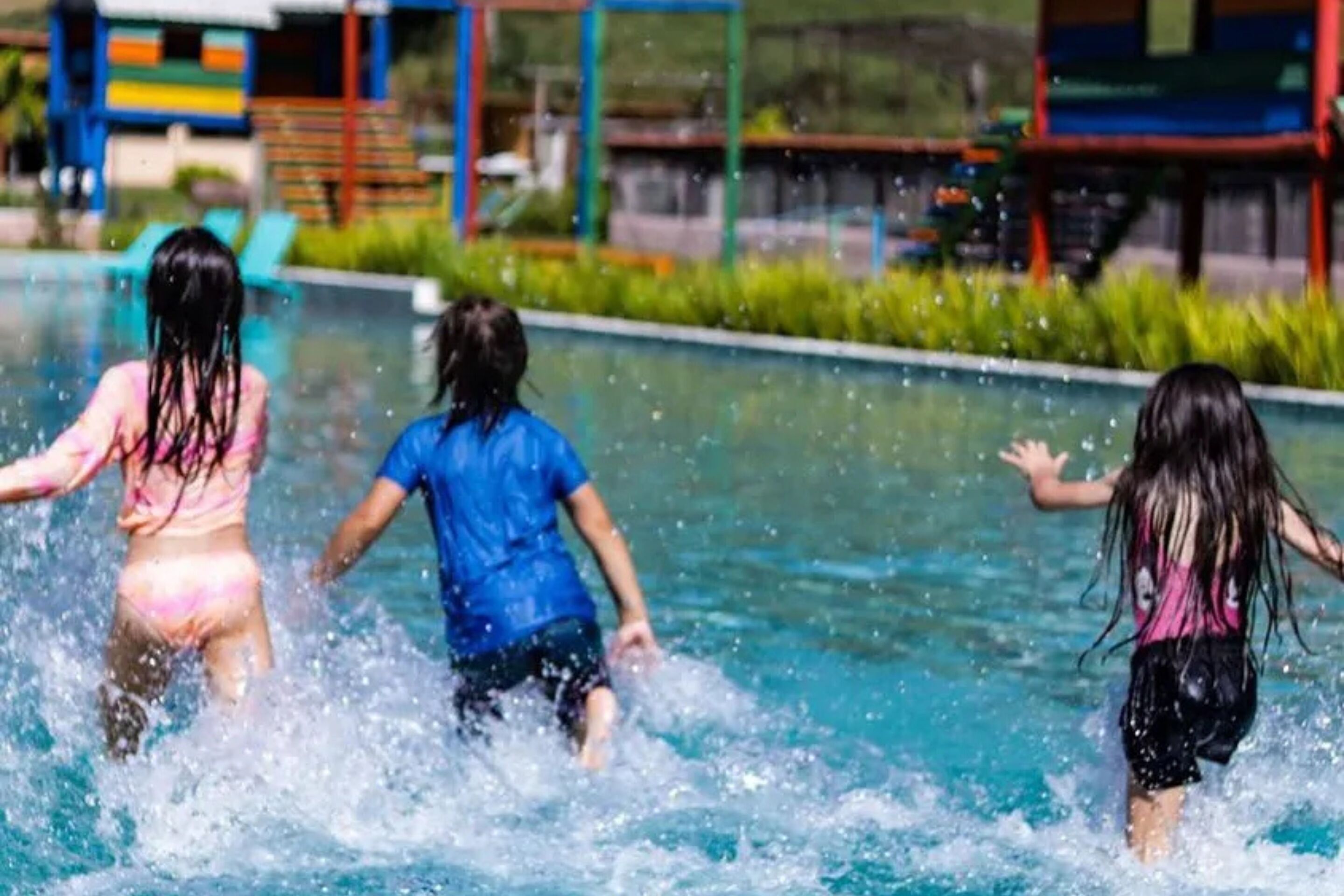 Uma piscina com três crianças brincando na água.
