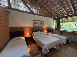 Quarto com duas camas individuais, piso de madeira, parede de tijolos e janela com vista para o verde.