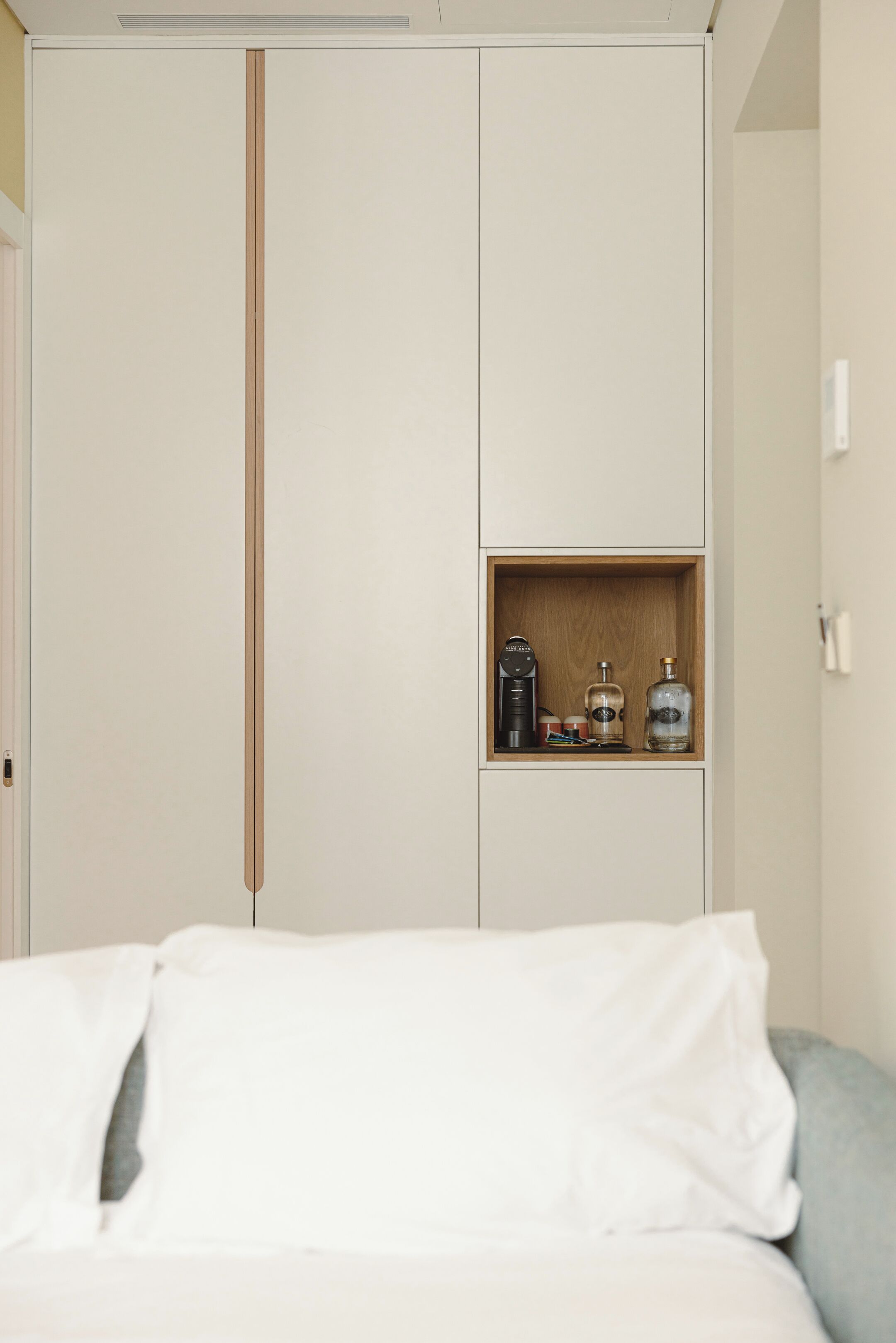 Quarto com cama, guarda-roupa e prateleira com cafeteira, garrafa de vidro e um recipiente.