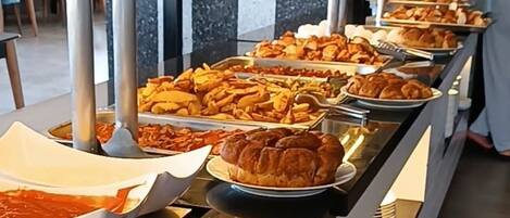 Buffet com diversos alimentos, incluindo doces, pães e acompanhamentos.