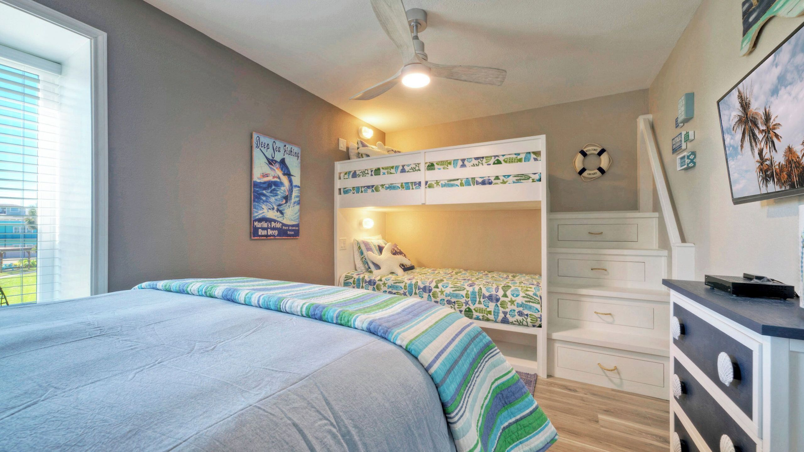 Quarto com cama beliche, ventilador de teto, um pôster e televisão na parede.
