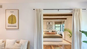 Um interior moderno com piso de madeira, um sofá com almofadas estampadas, uma cama com vista e uma obra de arte emoldurada na parede.