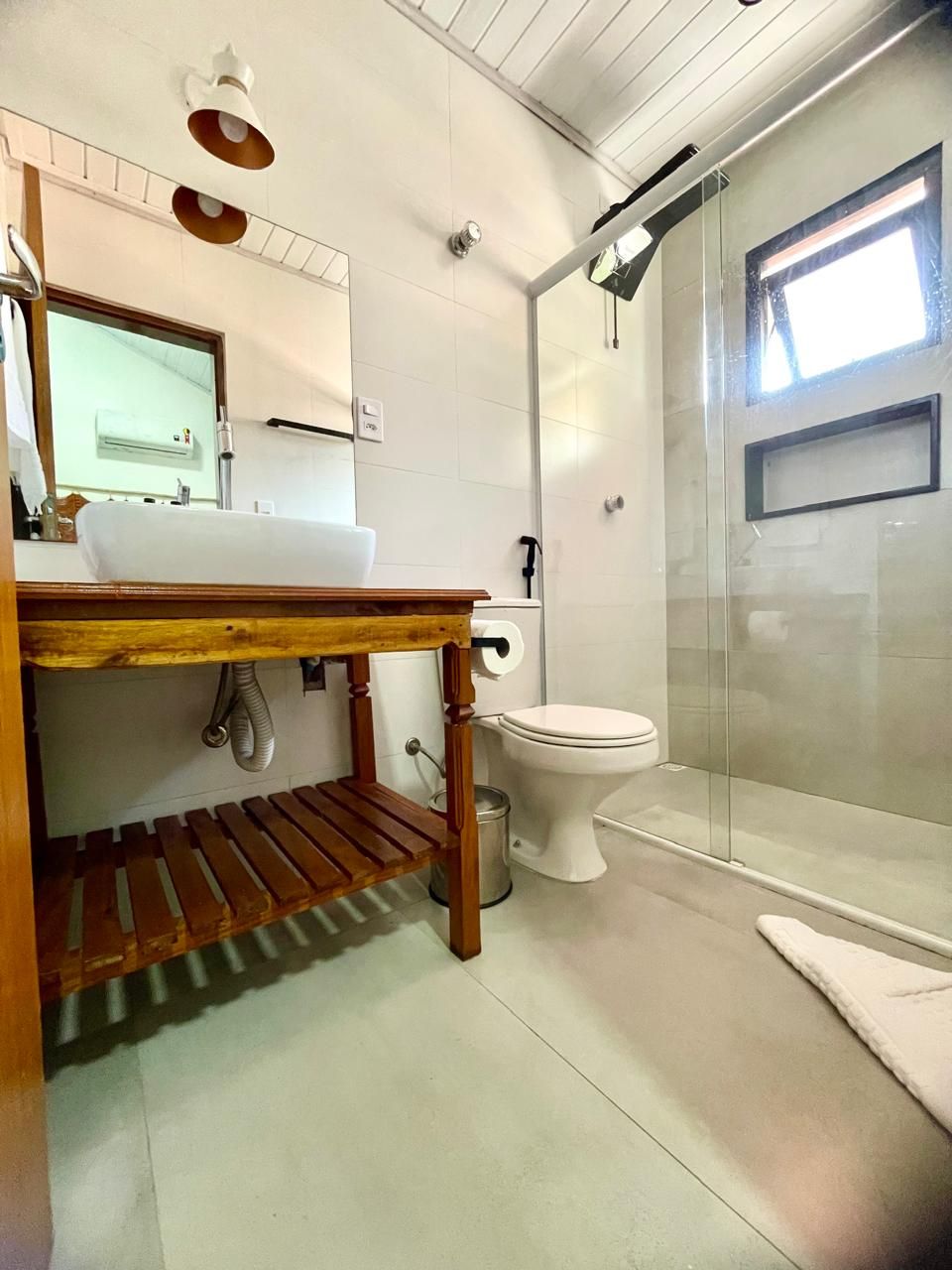 Casa de banho com toucador de madeira, lavatório branco e sanita.