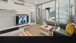 Uma sala de estar moderna com uma TV de tela plana, um sofá, uma mesa de centro e uma grande janela com vista para o exterior.