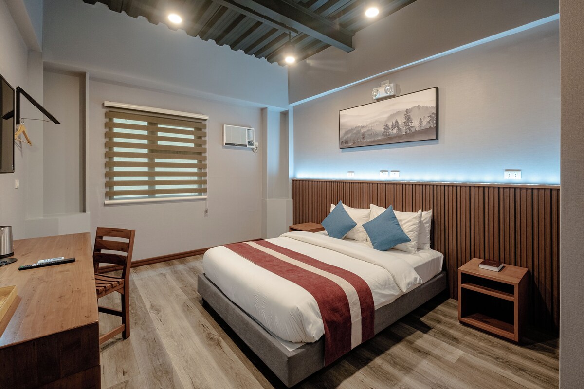 Um quarto com uma cama, mesas de cabeceira, uma escrivaninha e uma cadeira.