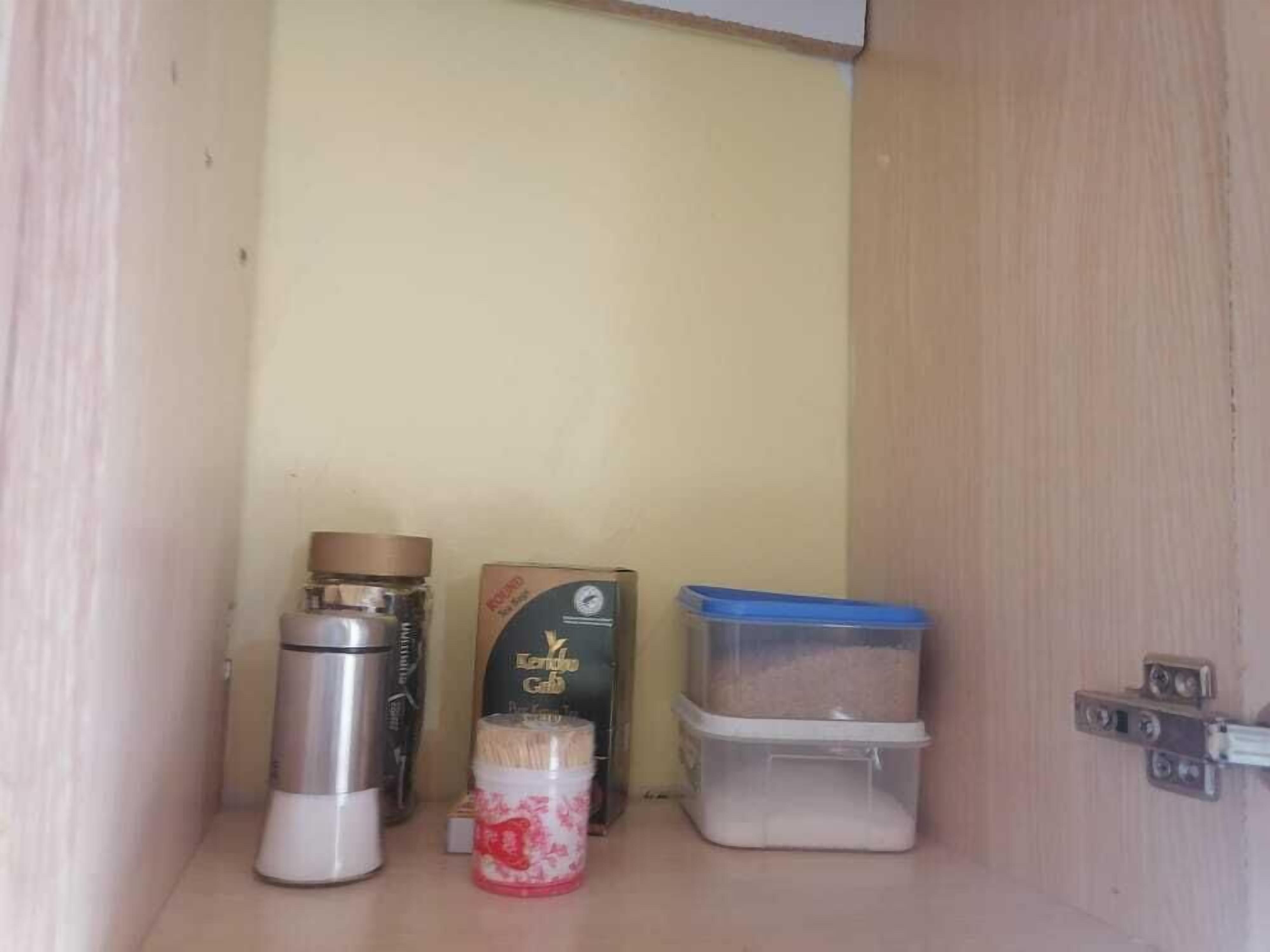 Um pequeno espaço de armazenamento com um termo de aço inoxidável, uma caixa com a etiqueta 'Kaffee Gabel' e um recipiente de plástico com tampa.