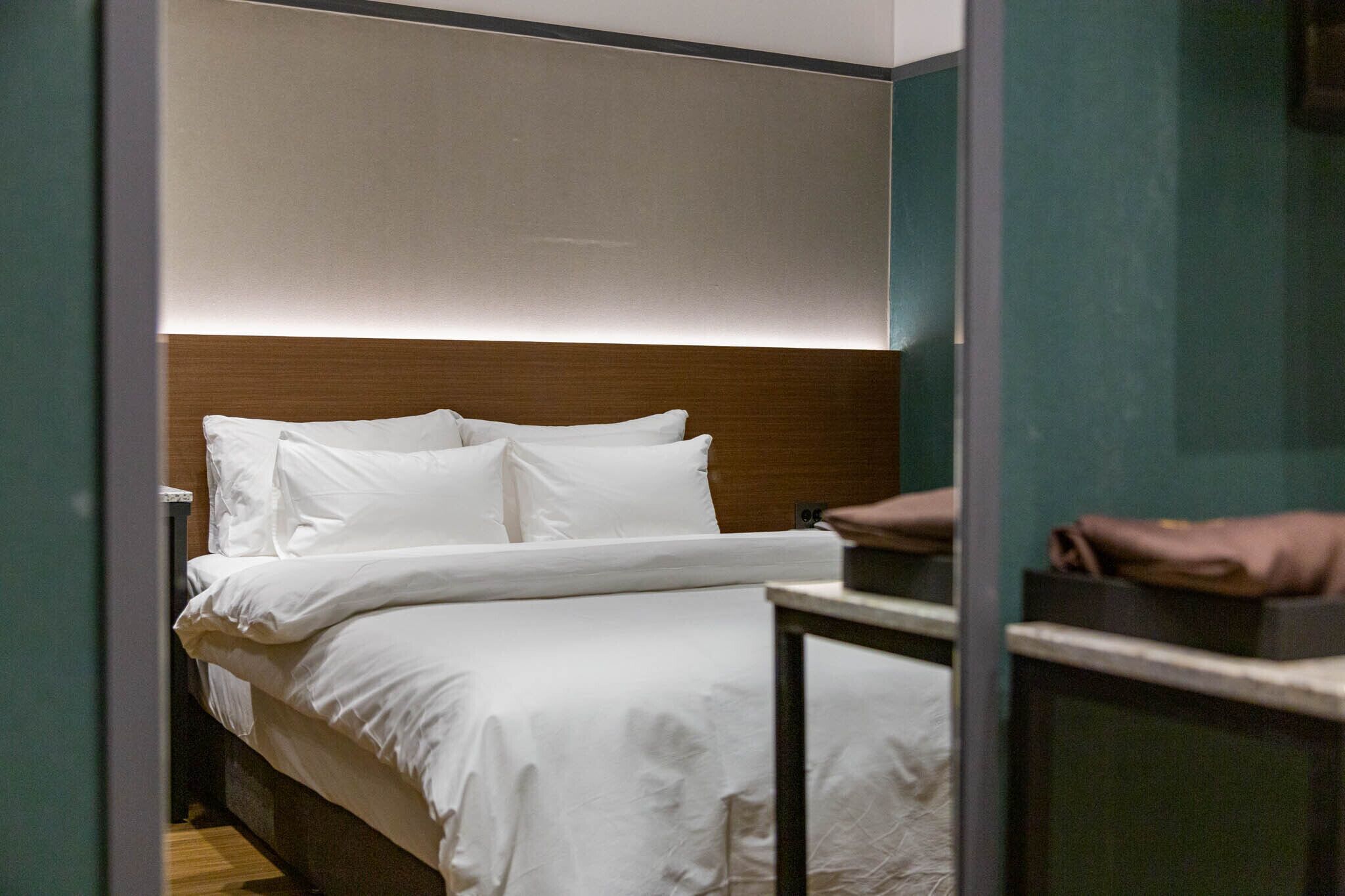 Quarto de hotel com cama, mesa de cabeceira e luminária fixada na parede.