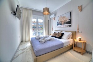 Um quarto moderno com uma cama grande, televisão montada na parede, um quadro e uma pequena mesa de cabeceira de madeira.