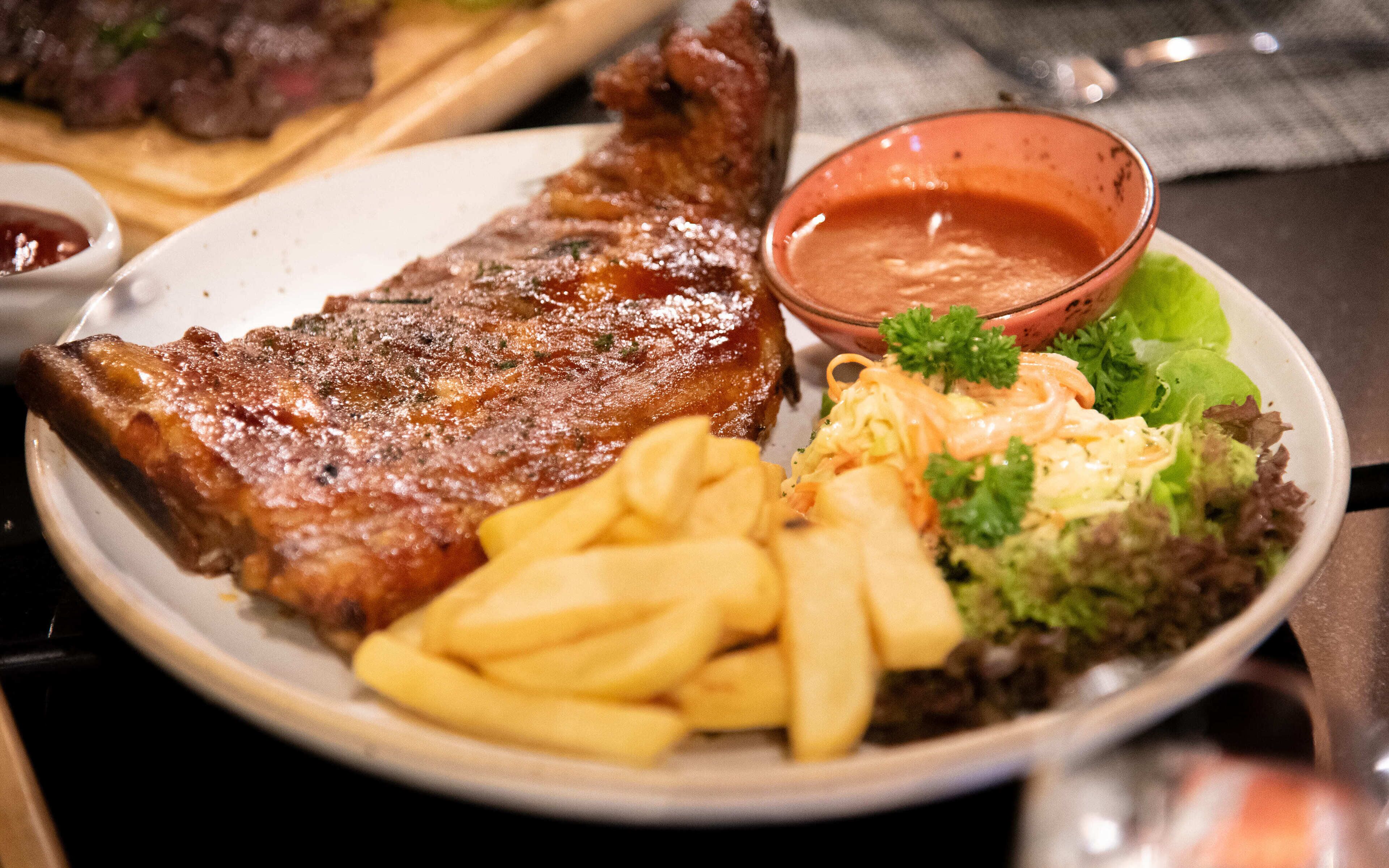 Um prato com bife, batatas fritas, salada e molho.