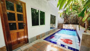 Uma área de piscina com piso revestido, uma porta de madeira e janelas.