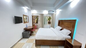 Quarto de hotel com cama, mesas de cabeceira, escrivaninha com cadeira, pequeno frigorífico e televisão fixada na parede.