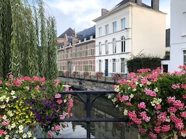 Um canal com uma ponte, rodeado por flores coloridas e arquitetura europeia tradicional.