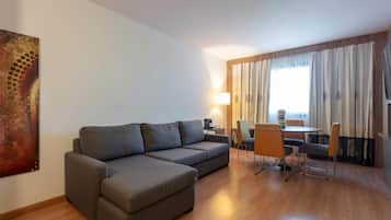 Uma sala moderna com um sofá seccional, uma mesa de jantar com cadeiras, um abajur e uma grande janela com cortinas.