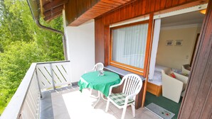 Uma varanda com mesa e cadeiras, interior em madeira e vista para o verde.
