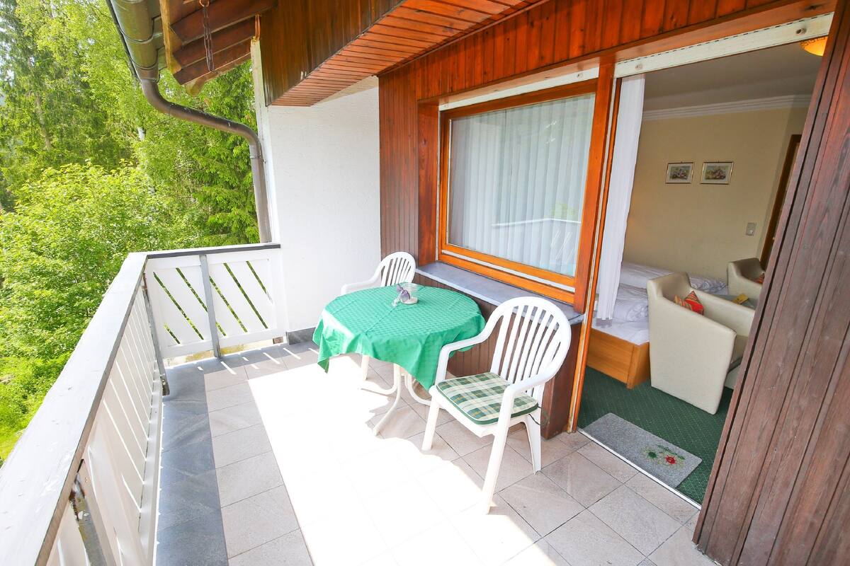 Uma varanda com mesa e cadeiras, interior em madeira e vista para o verde.