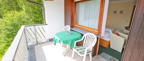 Uma varanda com mesa e cadeiras, interior em madeira e vista para o verde.