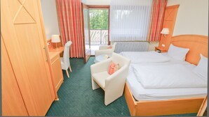 Quarto de hotel com cama, cadeira, escrivaninha, janela com cortinas e radiador.