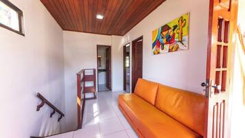 Quarto com teto de madeira, um sofá, um quadro e uma porta.