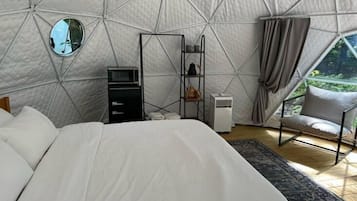 Quarto com cama, televisão, estante com objetos, cadeira e janela.