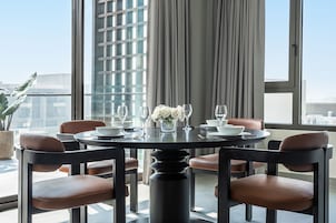 Uma sala de jantar com mesa redonda, seis cadeiras e um vaso de flores brancas.