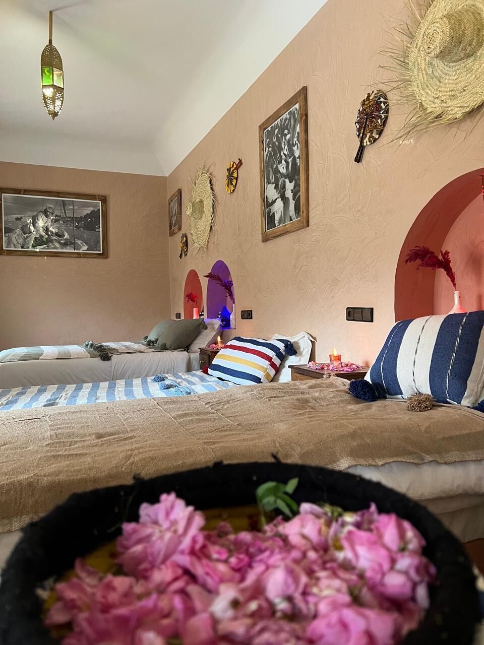 Quarto com duas camas, luminária pendente e decoração nas paredes, incluindo quadros e um objeto tecido grande.