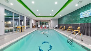 Piscina interior moderna com água azul cristalina, rodeada por cadeiras amarelas e uma parede verde de destaque.