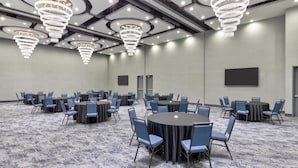 Uma sala de conferências com várias mesas e cadeiras, lustres no teto e uma tela grande na parede.