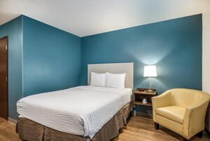 Quarto de hotel com cama, cadeira, mesa de cabeceira e abajur.