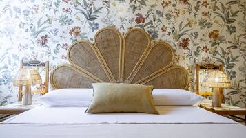 Uma cama com cabeceira original, duas luminárias de apoio e papel de parede floral.
