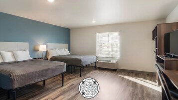 Quarto de hotel com duas camas, uma televisão e uma janela com persianas.