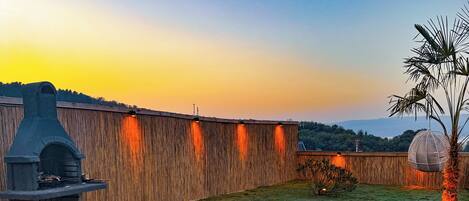 Um terraço no telhado com uma churrasqueira, um candeeiro decorativo e vista para o pôr do sol.