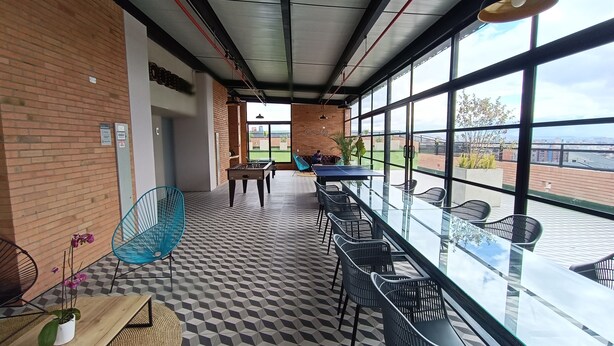 Espaço interior moderno com piso xadrez, mesas e cadeiras de vidro, e vista através de grandes janelas.