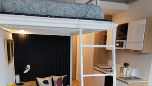 Um espaço compacto com cama mezanina, sofá, pequena área de refeições e cozinha compacta.