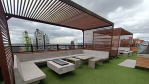 Terraço no telhado com área de estar moderna, grama sintética verde e vista do horizonte da cidade.