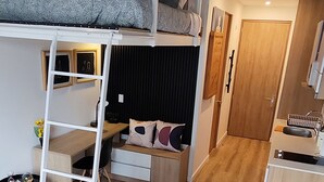 Quarto estilo loft com cama beliche, escrivaninha, cadeira e mesa pequena.