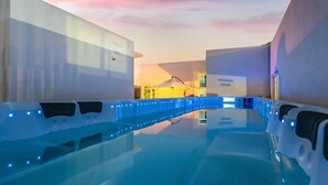 Piscina interna com luzes LED azuis nas bordas, rodeada por paredes brancas e um céu ao pôr do sol.