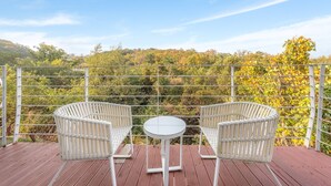Um deck de madeira com duas cadeiras de vime e uma pequena mesa redonda, com vista para uma área arborizada.