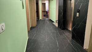 Um corredor com paredes verdes, soalho de mármore preto e portas de madeira.