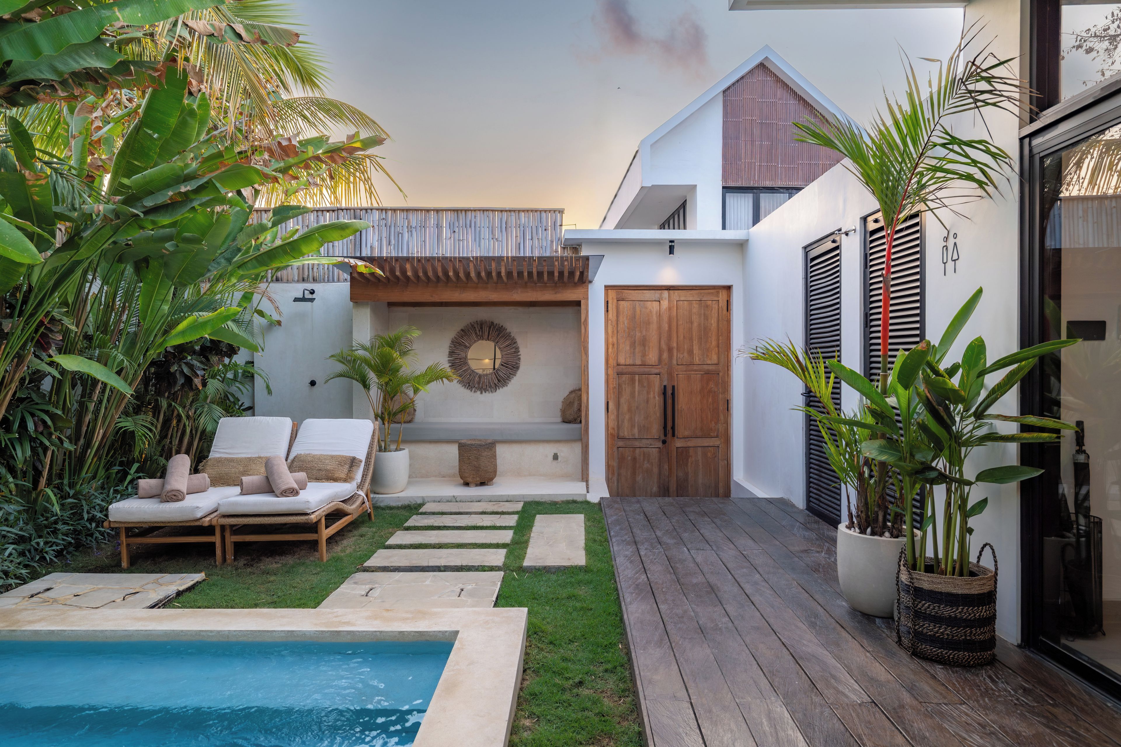 Uma área de piscina moderna ao ar livre, com espreguiçadeiras, deck de madeira e vegetação exuberante.