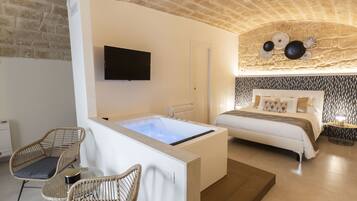 Quarto moderno com cama grande, banheira, cadeiras de vime e televisão de tela plana.