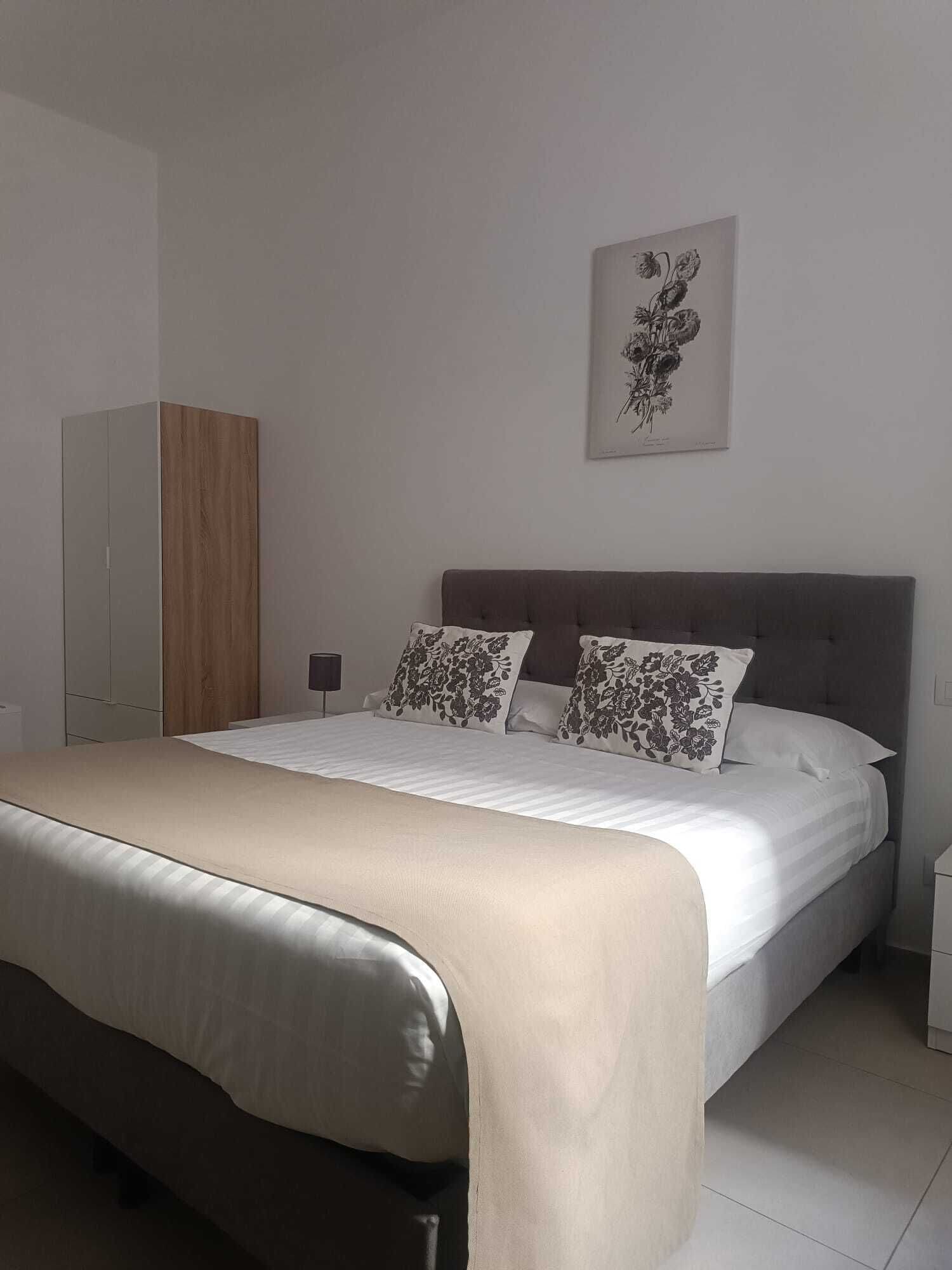 Quarto com cama, mesa de cabeceira, guarda-roupa e obra de arte na parede.