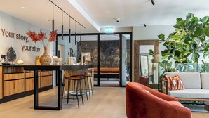 Um saguão de hotel moderno com uma receção, área de estar e uma grande planta.
