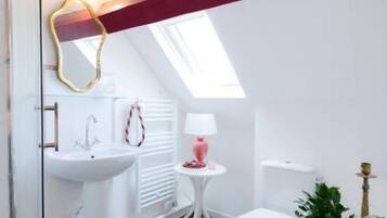 Uma casa de banho moderna com clarabóia, loiças sanitárias brancas e chão de madeira.