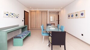 Uma zona de refeições moderna com mesa de vidro, cadeiras azuis e um banco com livros.