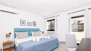 Quarto moderno com cama, mesas de cabeceira, uma cadeira e vista para o exterior.