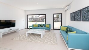 Uma sala de estar moderna com uma televisão de tela plana, um sofá azul, uma mesa de centro e um tapete estampado.